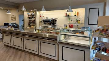 Um café com um balcão comprido, uma máquina de café e prateleiras com diversos produtos.