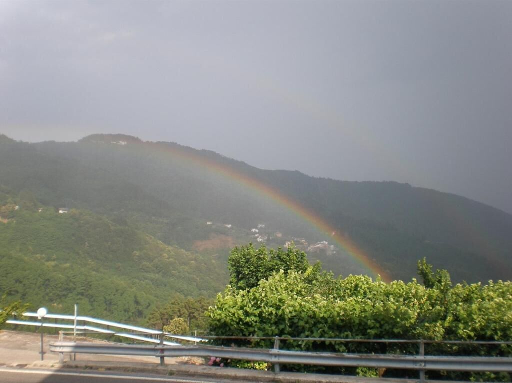 Paisagem montanhosa com um arco-íris sobre uma estrada.