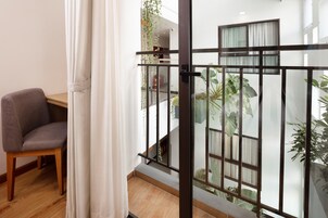 Quarto com cadeira de madeira, porta de vidro com estrutura metálica e vista para uma varanda com plantas.