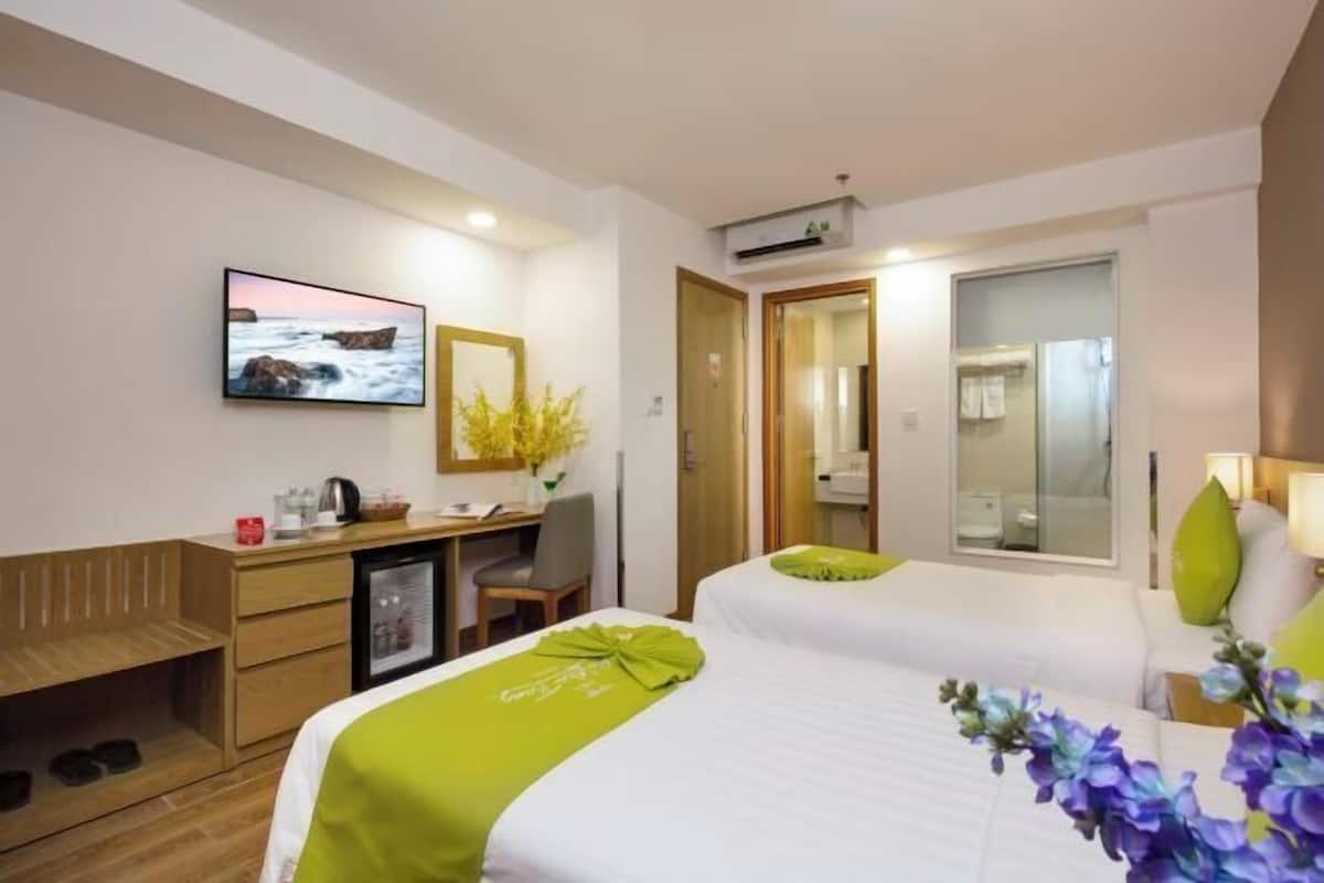 Quarto de hotel com duas camas, uma escrivaninha, uma cadeira, uma televisão e um espelho.
