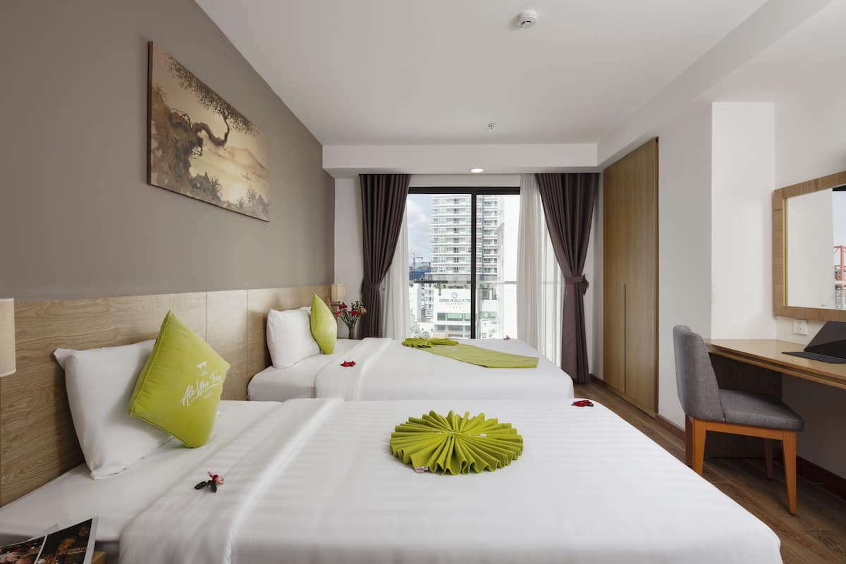 Quarto de hotel com duas camas, uma escrivaninha e uma janela grande com cortinas.