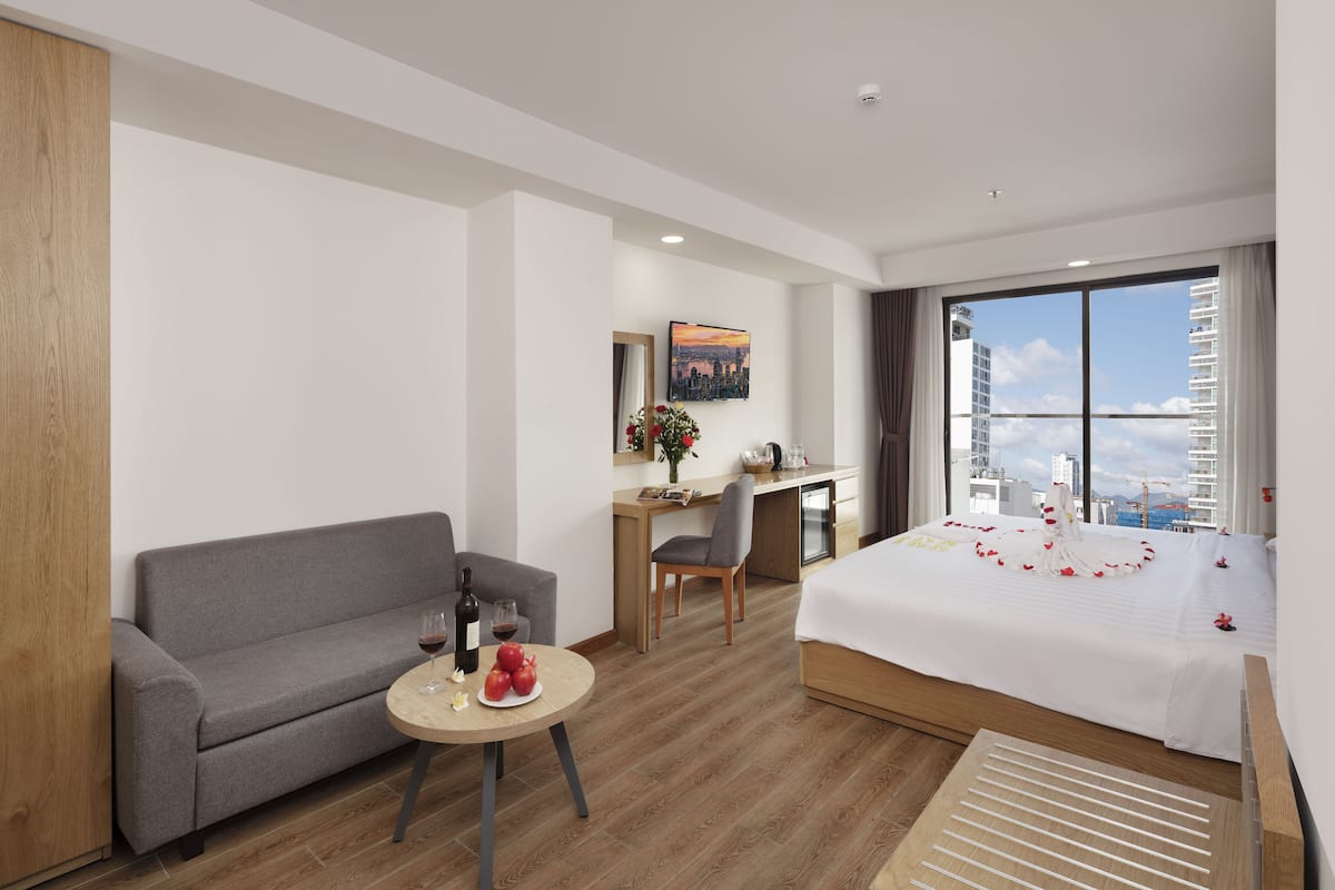 Quarto de hotel com cama, sofá, escrivaninha e vista da cidade.