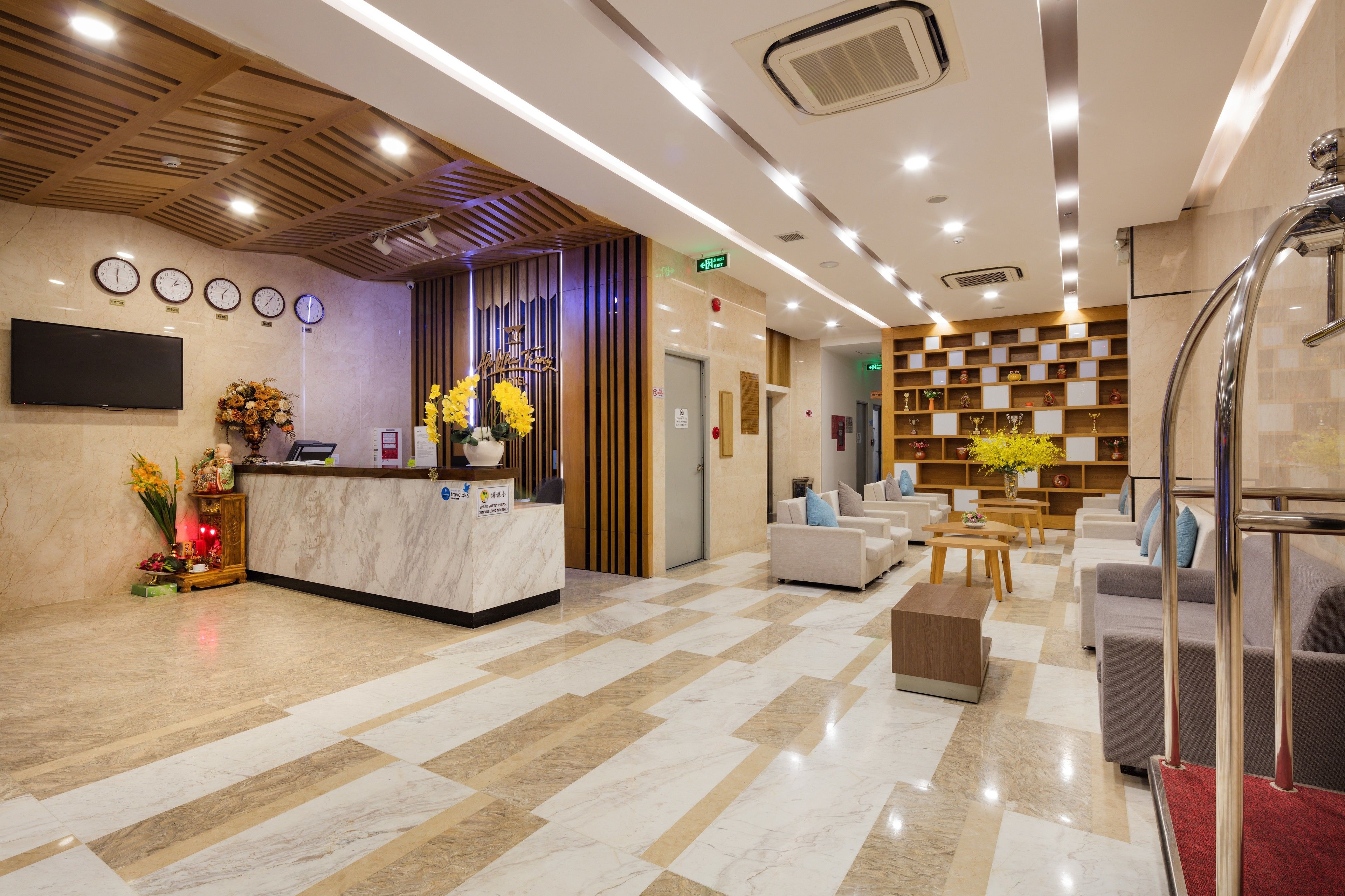 Um saguão de hotel com balcão de recepção, área de estar e uma parede com relógios.