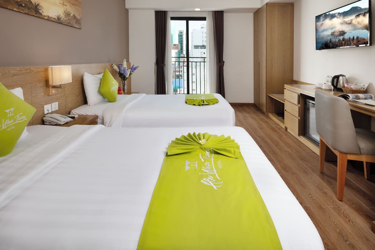 Quarto de hotel com duas camas, uma mesa, uma cadeira e varanda com vista para a cidade.