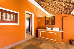 Casa de banho com parede laranja, teto de madeira, pia com espelho e porta que dá para outro quarto.