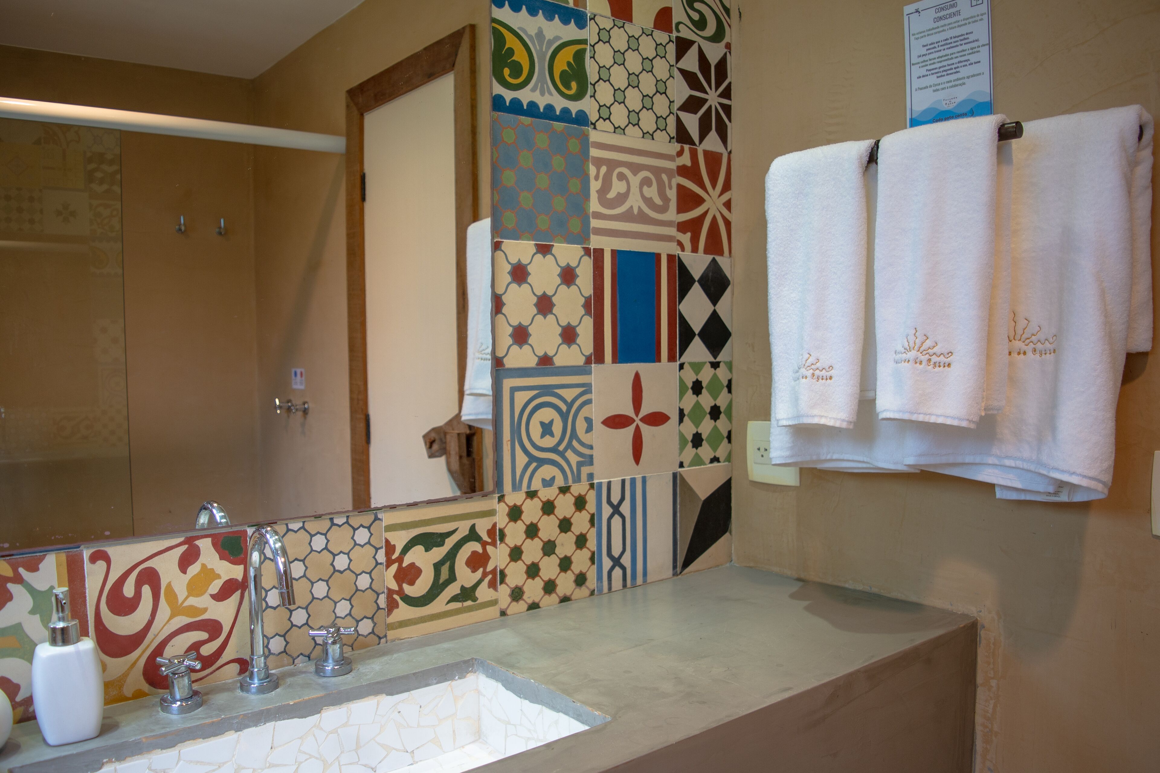 Casa de banho com revestimento de azulejos, lavatório com duas torneiras e um porta-toalhas com toalhas.