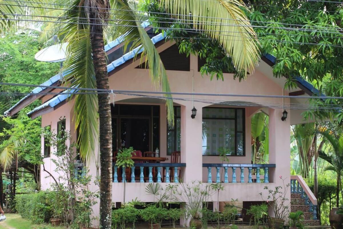 Uma casa de dois andares com varanda, rodeada por vegetação exuberante.