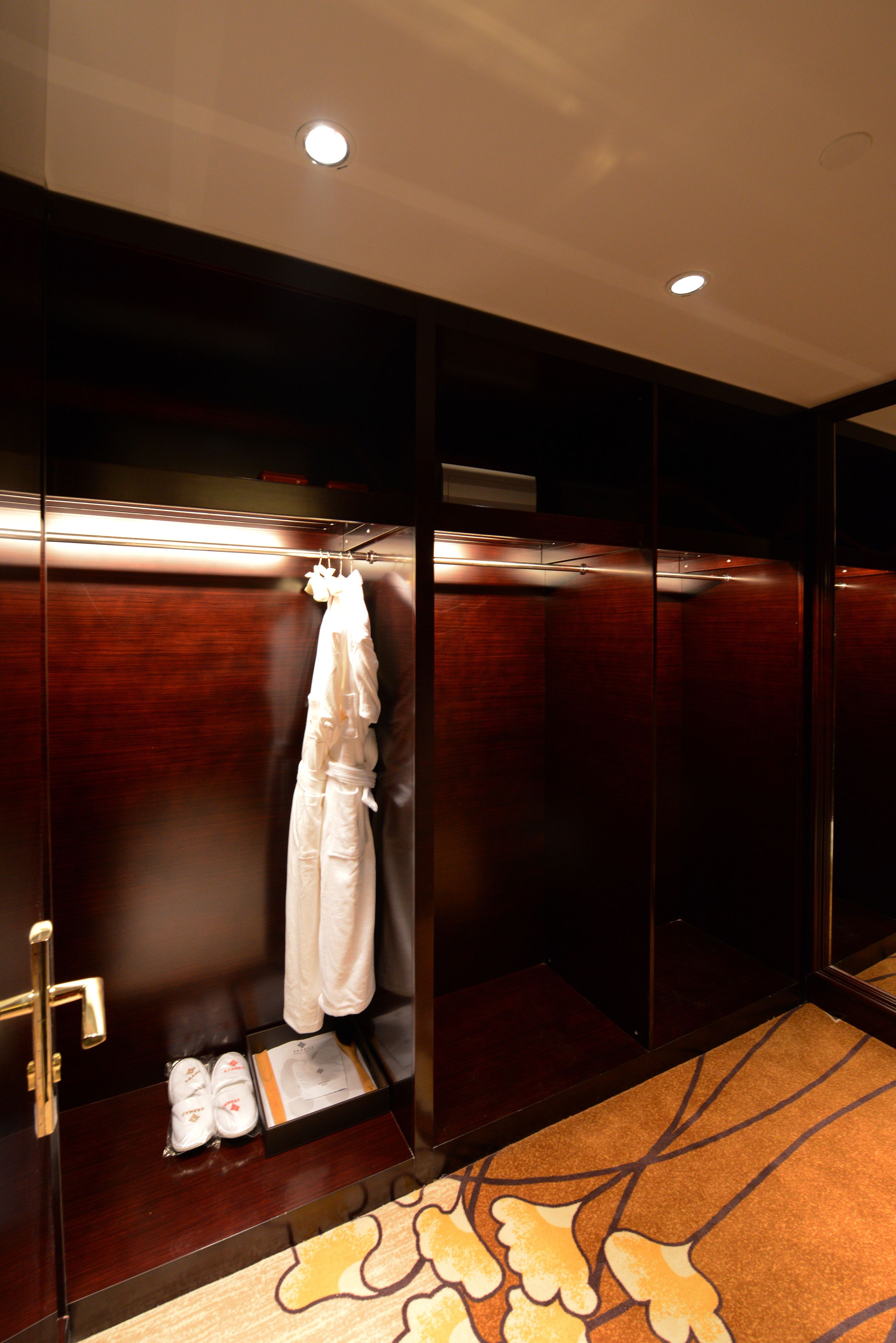 Quarto de hotel com um guarda-roupa de madeira, um roupão pendurado na porta e um par de chinelos no chão.