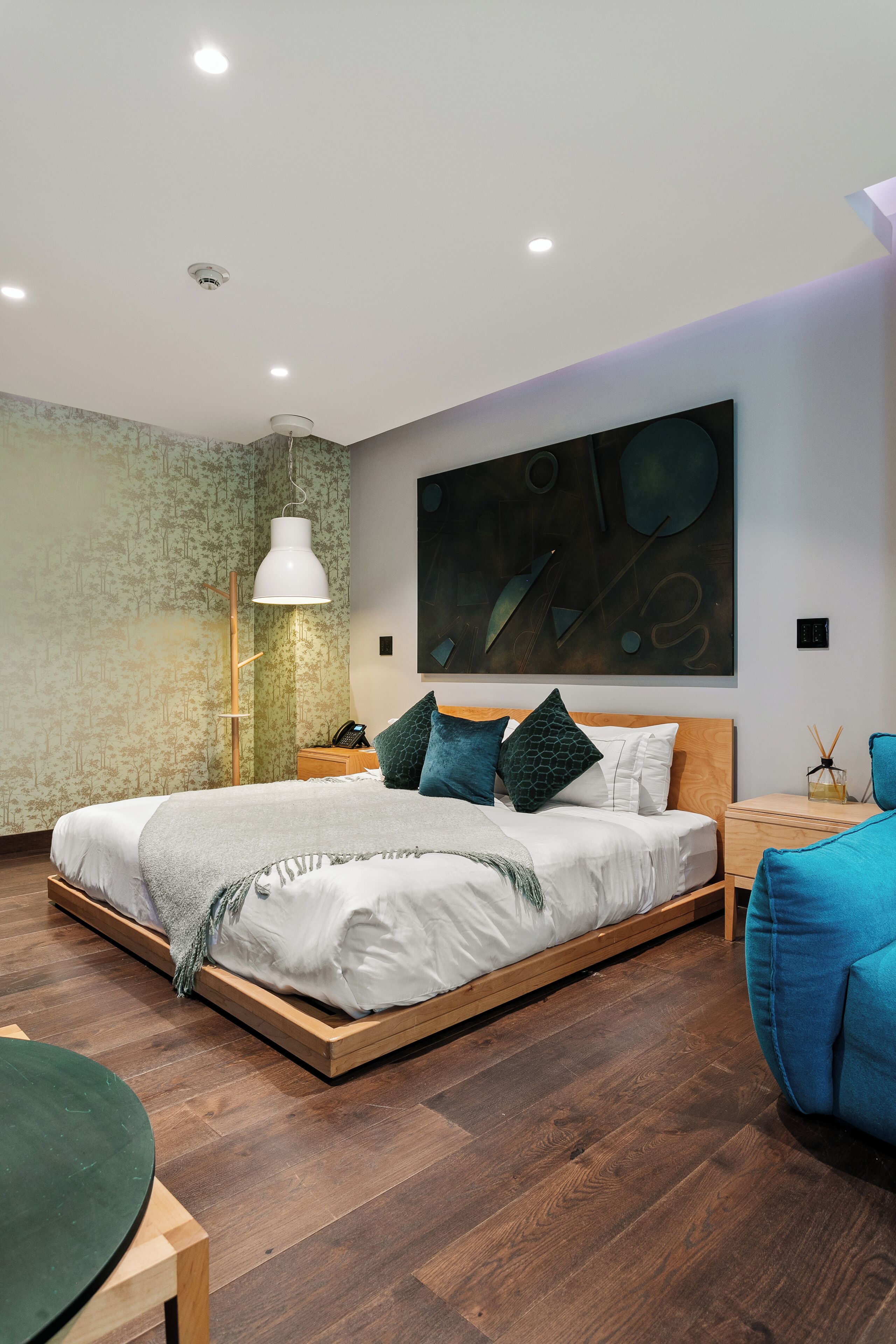 Quarto moderno com estrutura de cama de madeira, uma grande pintura abstrata e uma cadeira verde.