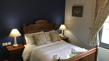 Cama bem arrumada com lençóis brancos, duas luminárias de cabeceira e cabeceira de madeira.
