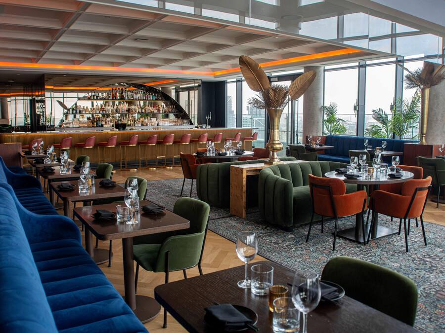 Restaurante moderno com bar, áreas de estar e amplas janelas com vista para a cidade.