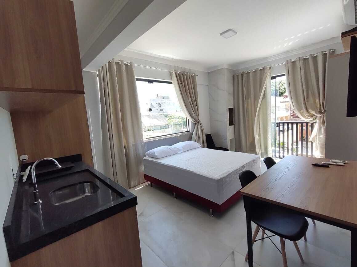 Quarto de hotel com cama, secretária, cadeira, pia e cortinas.
