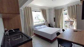 Quarto de hotel com cama, secretária, cadeira, pia e cortinas.