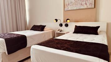 Quarto de hotel com duas camas de solteiro, uma mesinha de cabeceira com telefone, duas luminárias fixadas na parede e um quadro abstrato grande na parede.