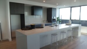 Uma cozinha moderna com uma ilha central, banquetas de bar e uma grande janela que proporciona iluminação natural.