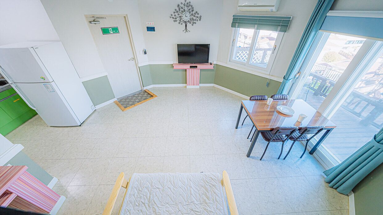 Quarto com mesa de jantar, cadeiras, televisão, refrigerador e janela com vista.