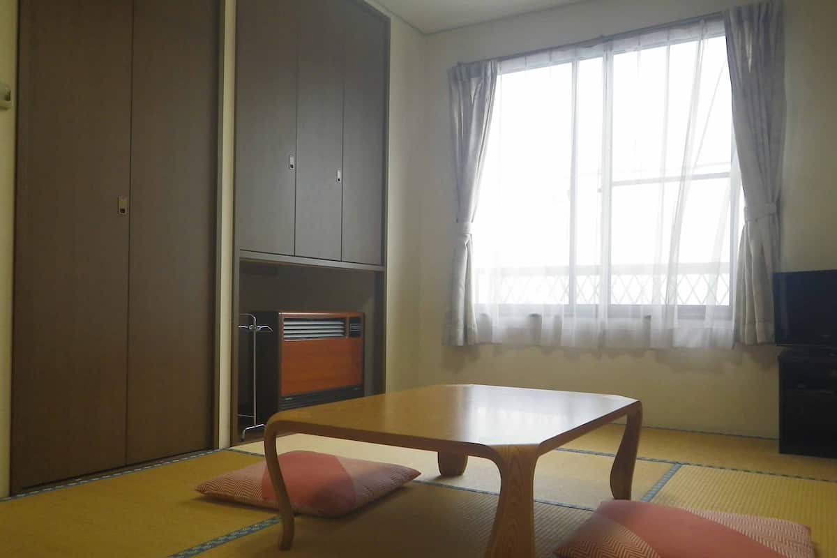 Quarto com piso de tatame, mesa de madeira, dois almofadas, televisão e guarda-roupa.