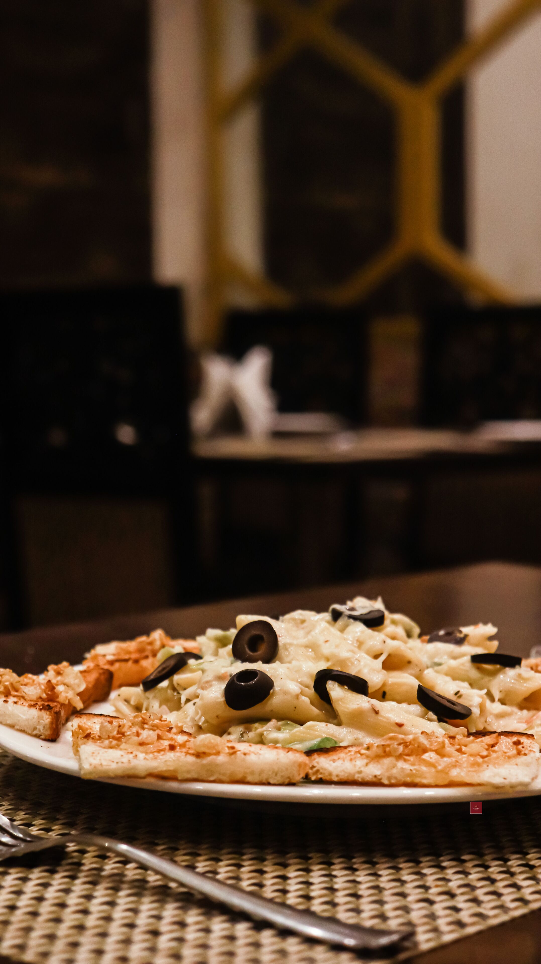 Pizza em um prato branco com um garfo ao lado, sobre um tapete de mesa trançado.