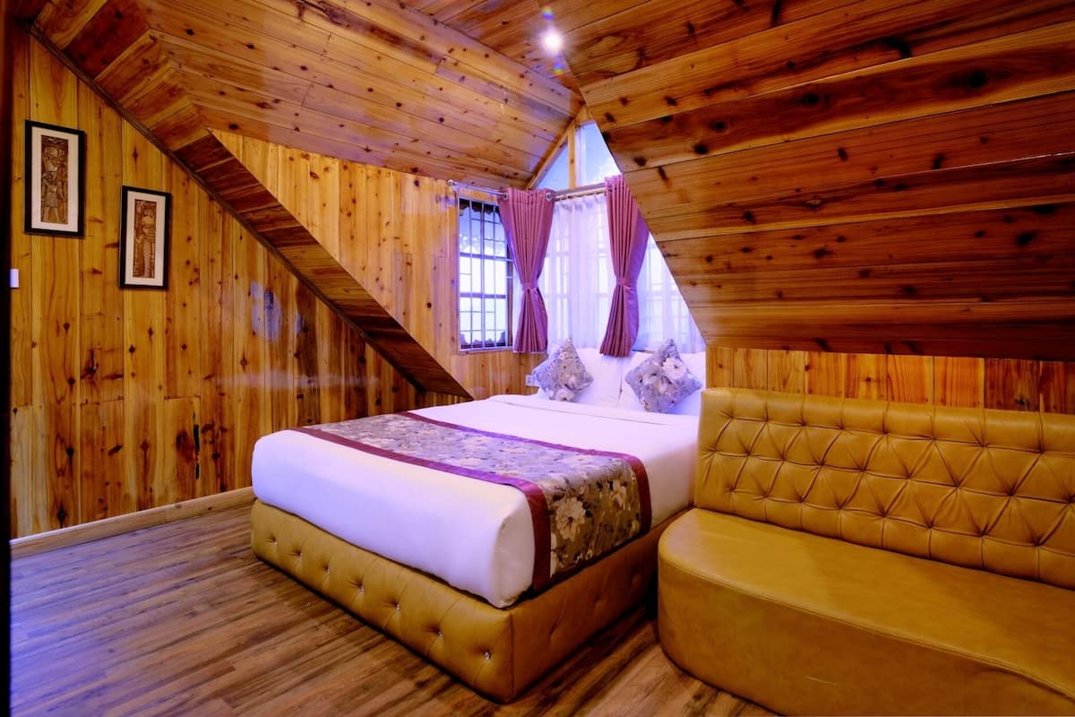 Um quarto de sótão acolhedor, com uma cama, um sofá, paredes de madeira e teto inclinado.