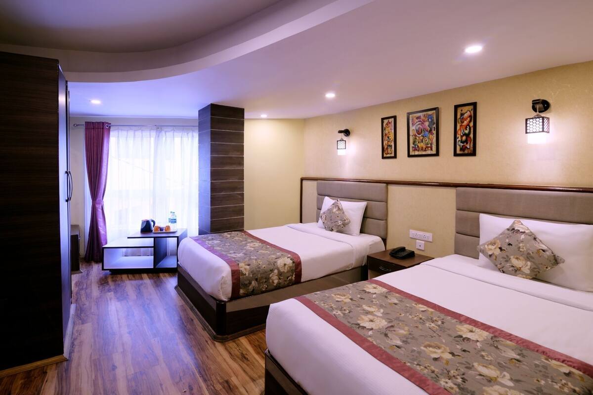 Quarto de hotel com duas camas, uma escrivaninha, uma cadeira, um guarda-roupa e um banheiro visível por uma porta aberta.