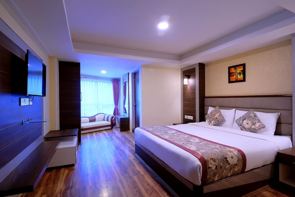Quarto de hotel com cama, televisão fixada na parede, sofá e porta para uma varanda.