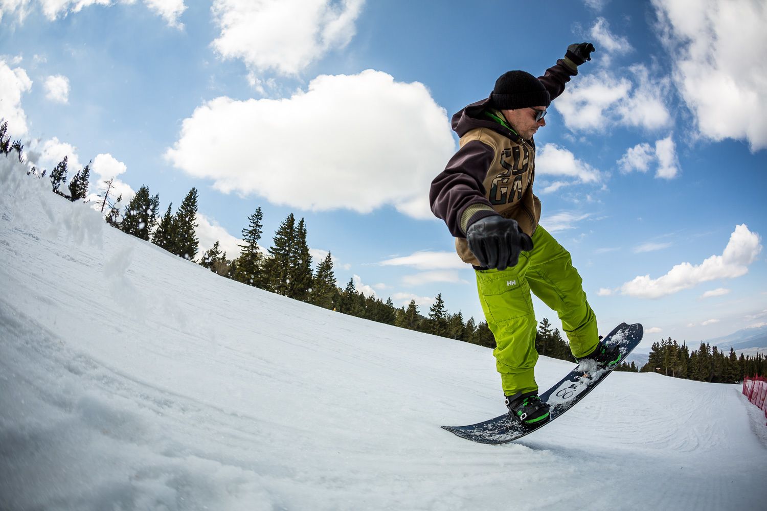 Um snowboarder em uma encosta nevada, com árvores ao fundo.