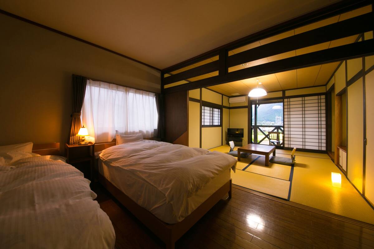 Quarto de hotel com duas camas, varanda, piso de tatame e vista para a montanha.
