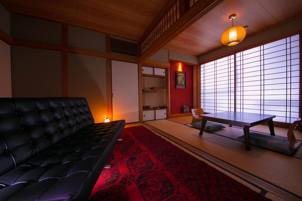 Um quarto japonês tradicional com tatames, um sofá preto, uma mesinha baixa e portas deslizantes.