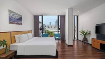 Quarto de hotel moderno com uma cama grande, televisão, planta e vista para a cidade.