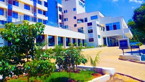 Um hotel moderno com vários andares, uma placa chamativa do Grand Royal Swiss Hotel, e uma área externa bem cuidada com vegetação.