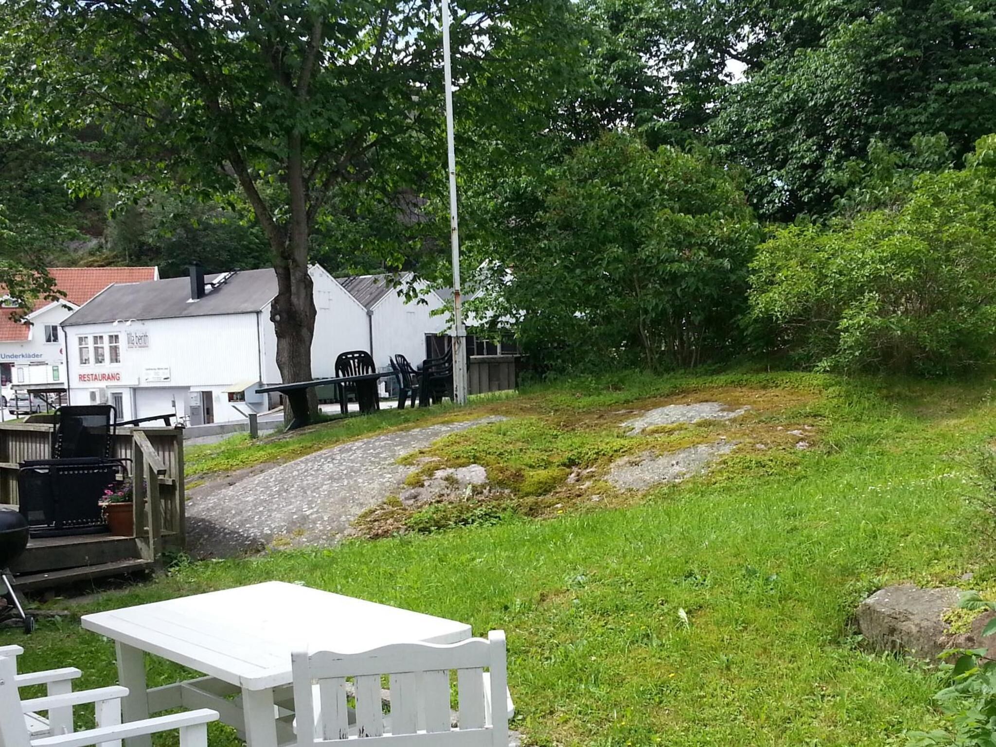 Uma área gramada com uma mesa e cadeiras brancas, uma churrasqueira e um edifício com uma placa que diz "RESTAURANG".