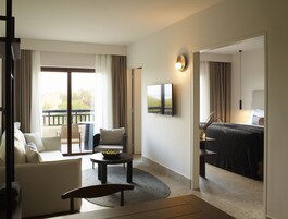 Quarto de hotel moderno com sofá, uma mesa pequena, televisão na parede e uma cama.