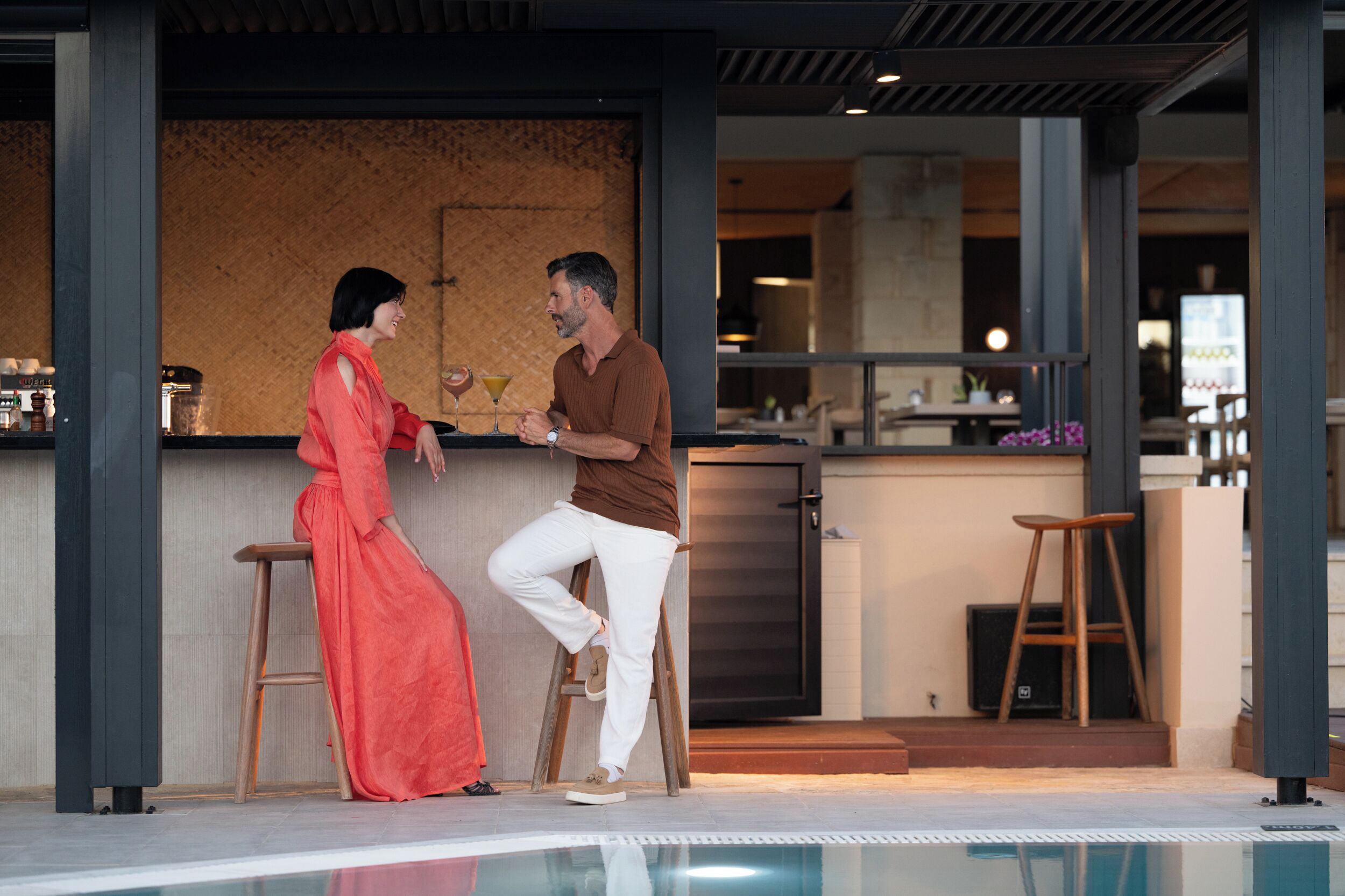 Um homem e uma mulher estão perto do bar à beira da piscina, com decoração moderna e vista clara para a piscina.