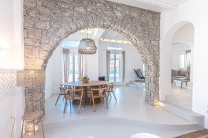 Um quarto espaçoso com um arco de pedra, uma mesa redonda de madeira com cadeiras, um lustre e vista para o exterior.