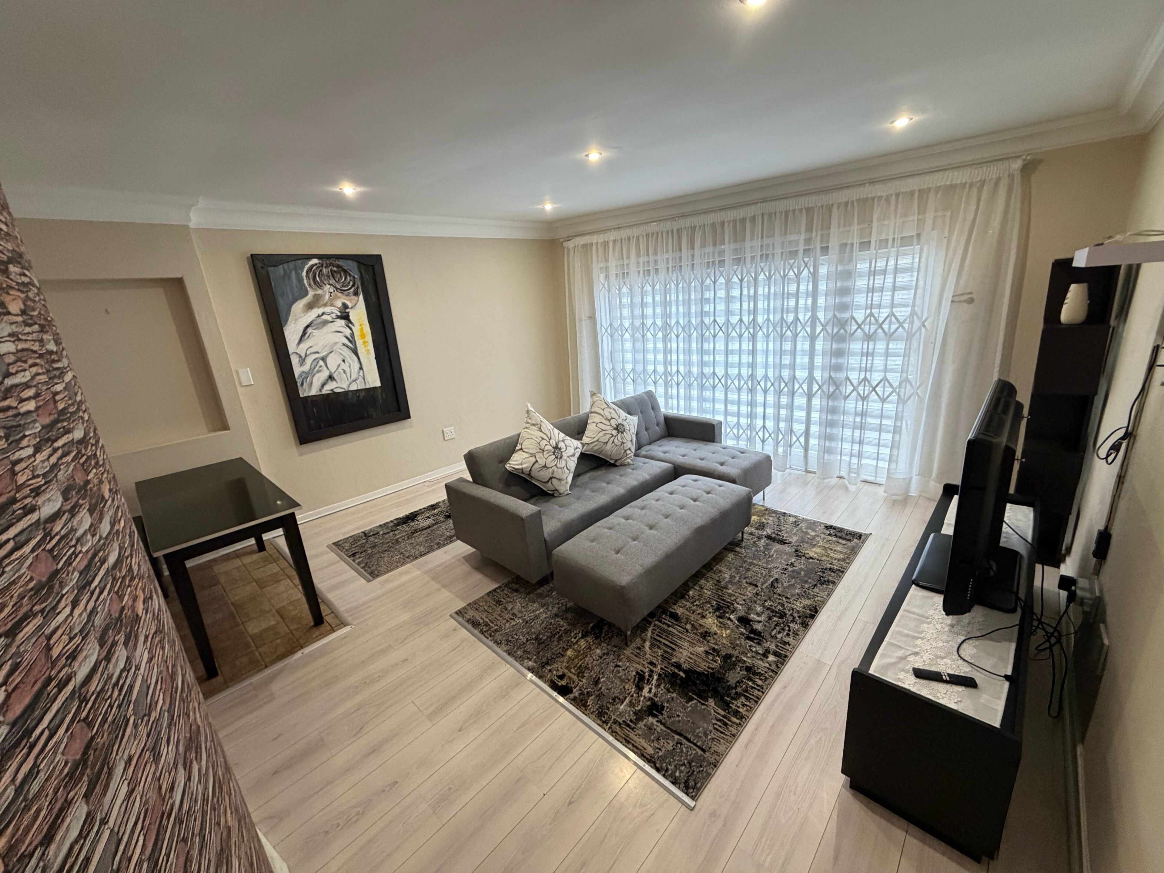 Uma sala de estar moderna com um sofá seccional cinza, uma TV de tela plana e uma grande janela com cortinas leves.