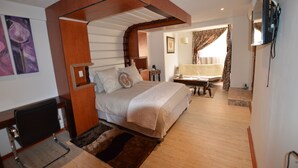Quarto com cama, escrivaninha, cadeira e televisão.