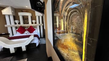 Quarto de hotel com cama, uma janela grande e vista para um corredor interno.