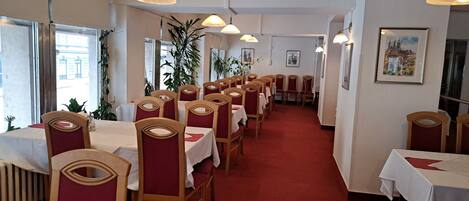 Um restaurante com fileiras de cadeiras e mesas de madeira, cadeiras com almofadas vermelhas e plantas em vasos.