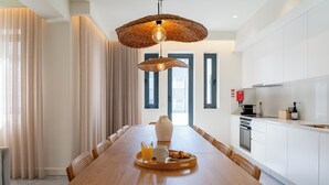 Uma área de refeições moderna com uma mesa de madeira, uma luminária pendente trançada e uma bandeja de café da manhã com suco e croissant.