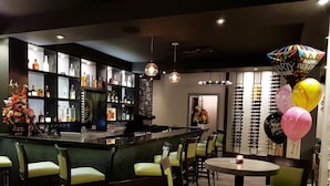 Uma área de bar com balcão, prateleiras cheias de garrafas e diversos assentos.
