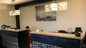 Uma área de recepção com duas bancadas de mármore, um lustre moderno e um quadro na parede.