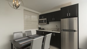 Uma cozinha moderna com armários escuros, eletrodomésticos de aço inoxidável, uma mesa de jantar com cadeiras e um lustre.