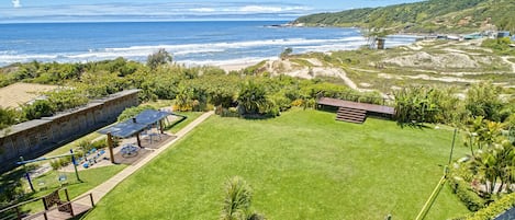 Um gramado bem cuidado com área de pátio, um pequeno deck e vista para o oceano.