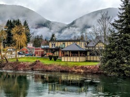 Um edifício à beira do lago, com um cais, rodeado por montanhas e árvores.