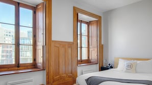 Quarto com uma cama grande, molduras de janela em madeira, um radiador e uma mesa de cabeceira com abajur.