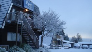 Uma pousada com escadas que levam a uma varanda, cercada por árvores cobertas de neve e carros estacionados.
