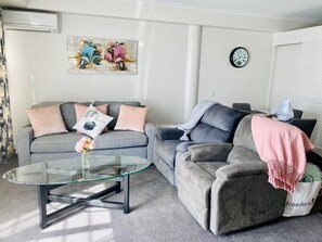 Sala de estar com sofá cinza, mesa de centro de vidro e quadro com scooters na parede.