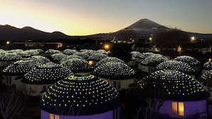 Vista de uma cidade com vários edifícios em formato de cúpula, cada um decorado com inúmeras luzes, e uma montanha imponente ao fundo.