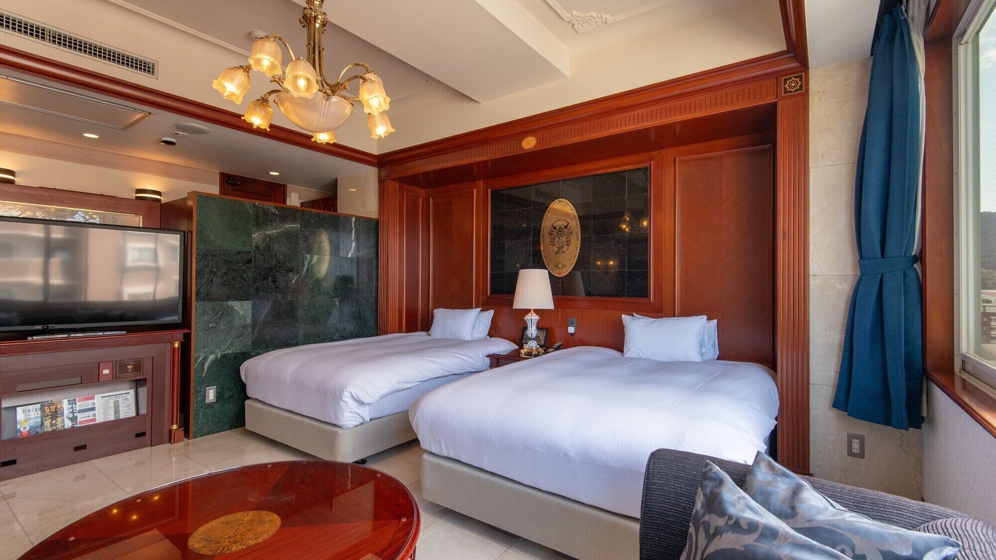 Quarto de hotel com duas camas, televisão, lustre e vista para a cidade.