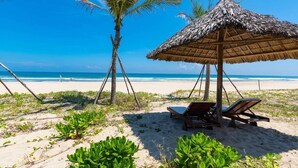 Uma praia com uma cabana de palha e cadeiras de descanso.
